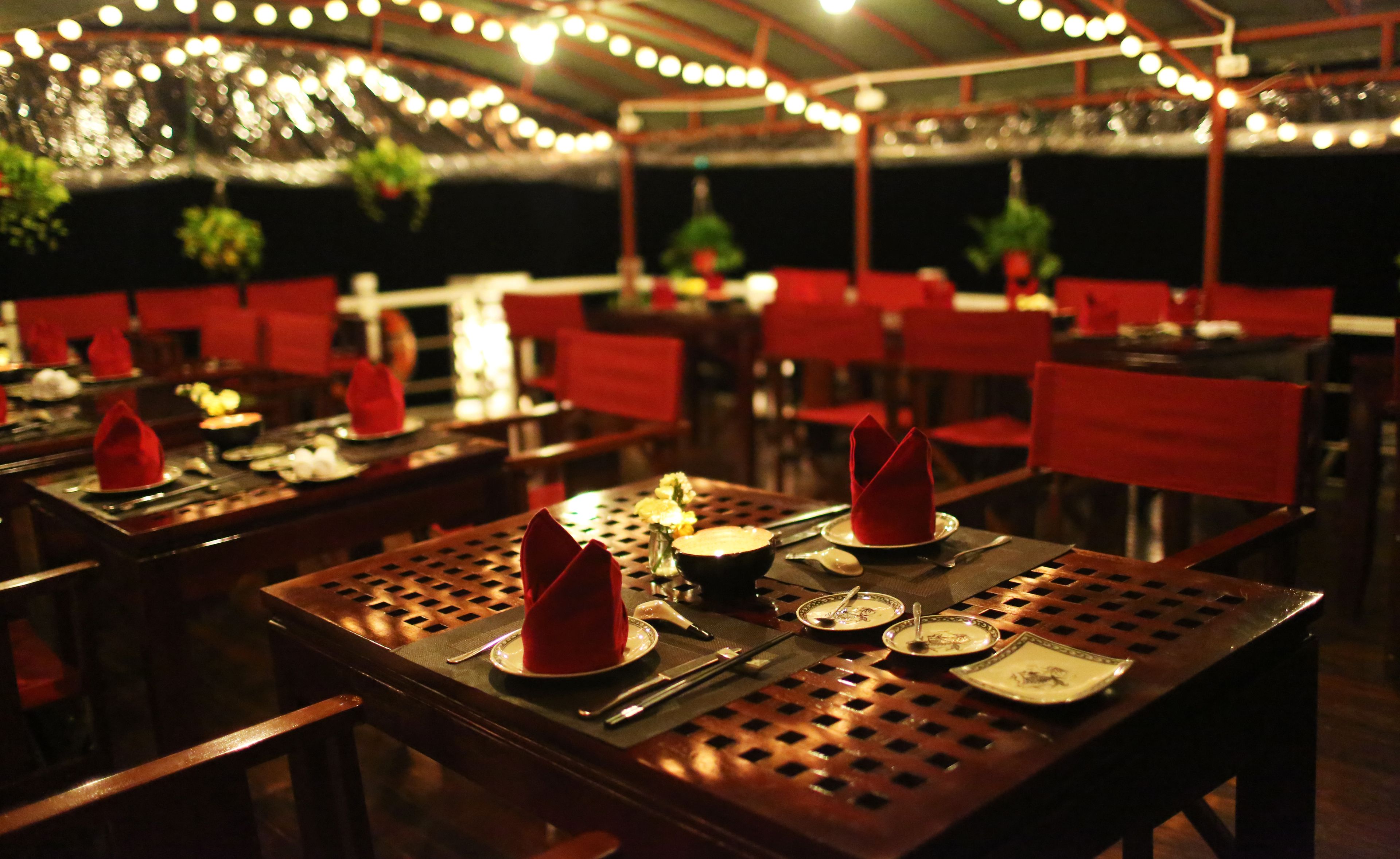 Restaurante ao ar livre com mesas preparadas para refeições, com ambiente acolhedor e luzes pendentes.