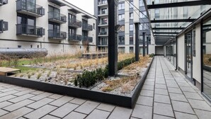 Um edifício moderno com várias varandas, uma galeria coberta e um jardim ajardinado.