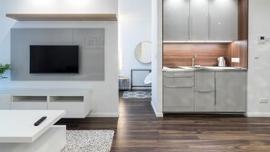 Uma sala de estar moderna com televisão de tela plana, móveis planejados para entretenimento e uma cozinha com armários de madeira e bancada.