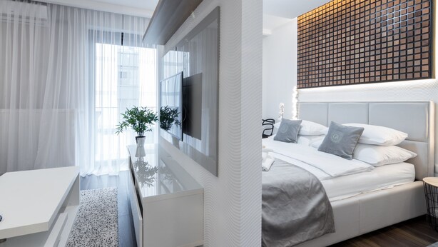 Quarto moderno com cama, mesa de cabeceira e TV fixada na parede.