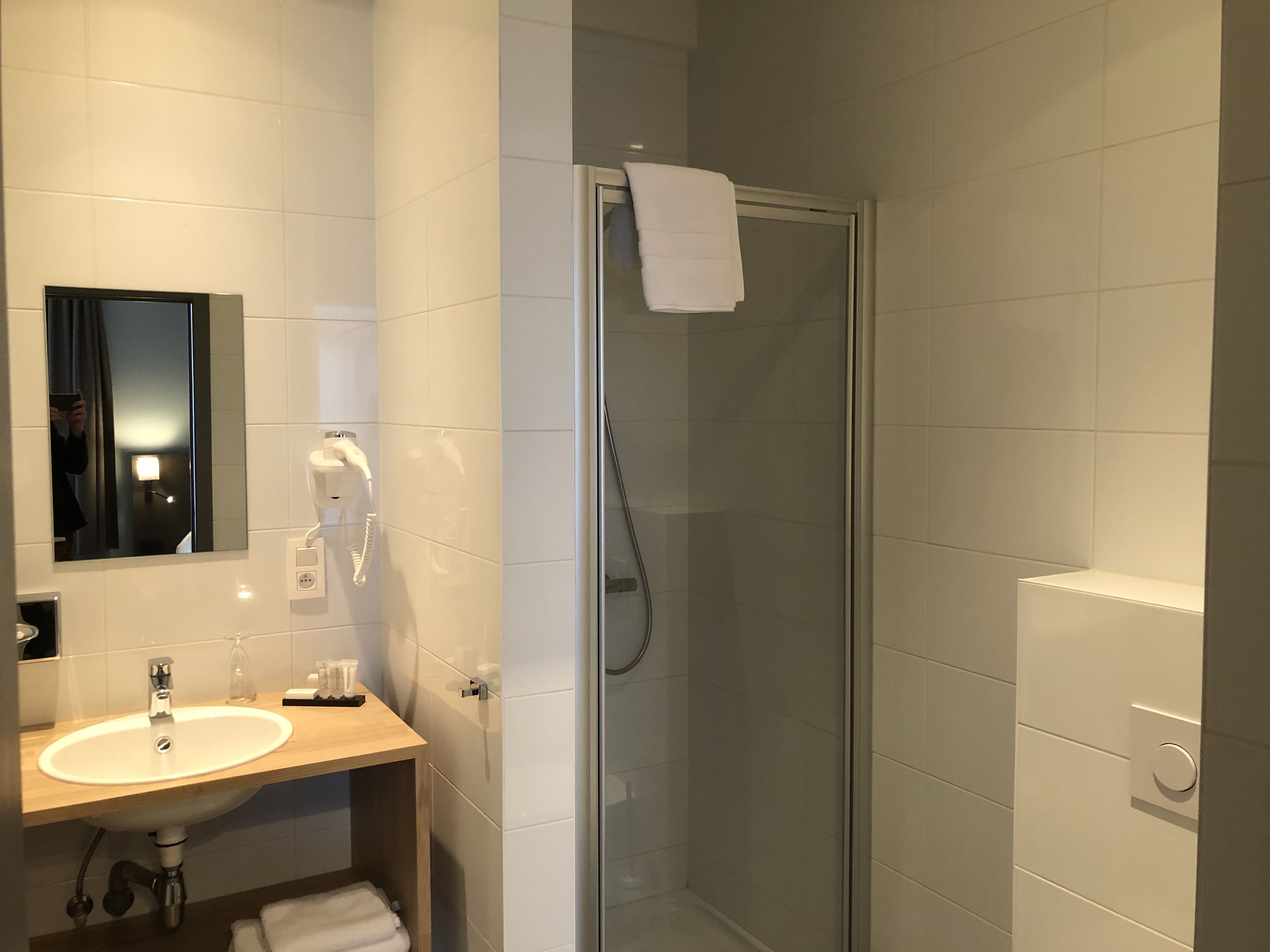 Um banheiro moderno com chuveiro em box de vidro, pia com espelho e porta-toalhas.