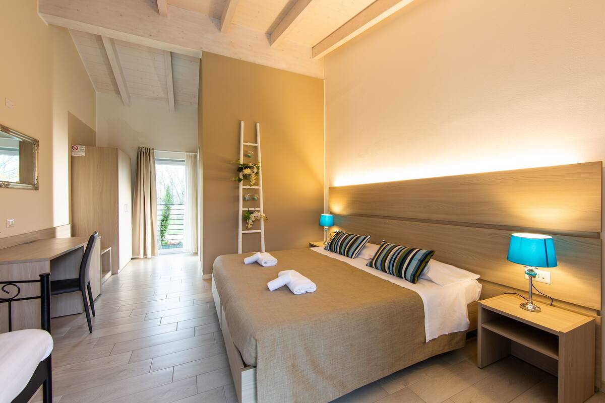 Quarto de hotel com cama, mesas de cabeceira, escrivaninha e uma cadeira.