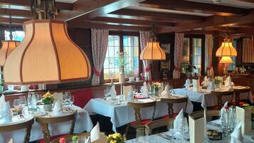 Restaurante com várias mesas preparadas para refeições, com toalhas brancas, talheres bem dispostos e luminárias pendentes.