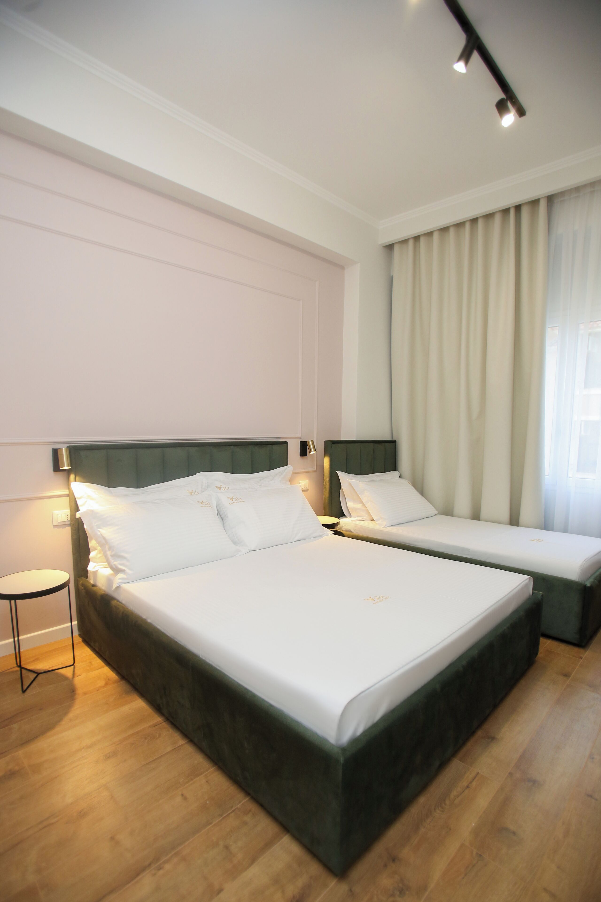 Quarto de hotel com duas camas de solteiro, uma mesa de cabeceira, um abajur e uma janela com cortinas.