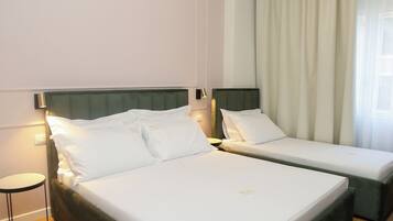 Quarto de hotel com duas camas de solteiro, uma mesa de cabeceira, um abajur e uma janela com cortinas.