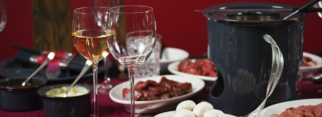 Uma mesa de jantar com copos de vinho, um bule quente e diversos pratos.