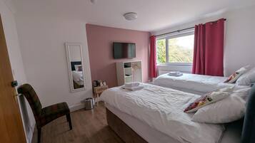 Quarto de hotel com duas camas, televisão, espelho, guarda-roupa e janela com cortinas.