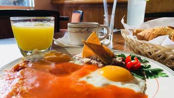 Prato de café da manhã com ovos, feijão refogado e torradas, acompanhado de um copo de suco de laranja e uma xícara de café.