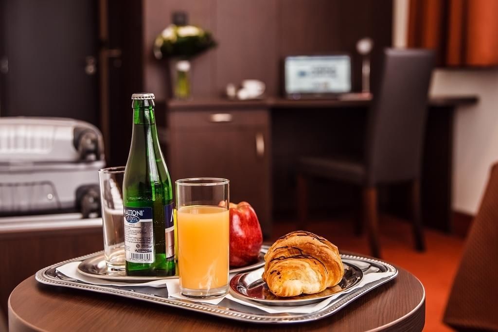 Bandeja de café da manhã com um croissant, suco de laranja e uma garrafa de água em um quarto de hotel.
