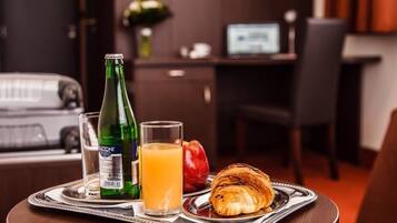 Bandeja de café da manhã com um croissant, suco de laranja e uma garrafa de água em um quarto de hotel.