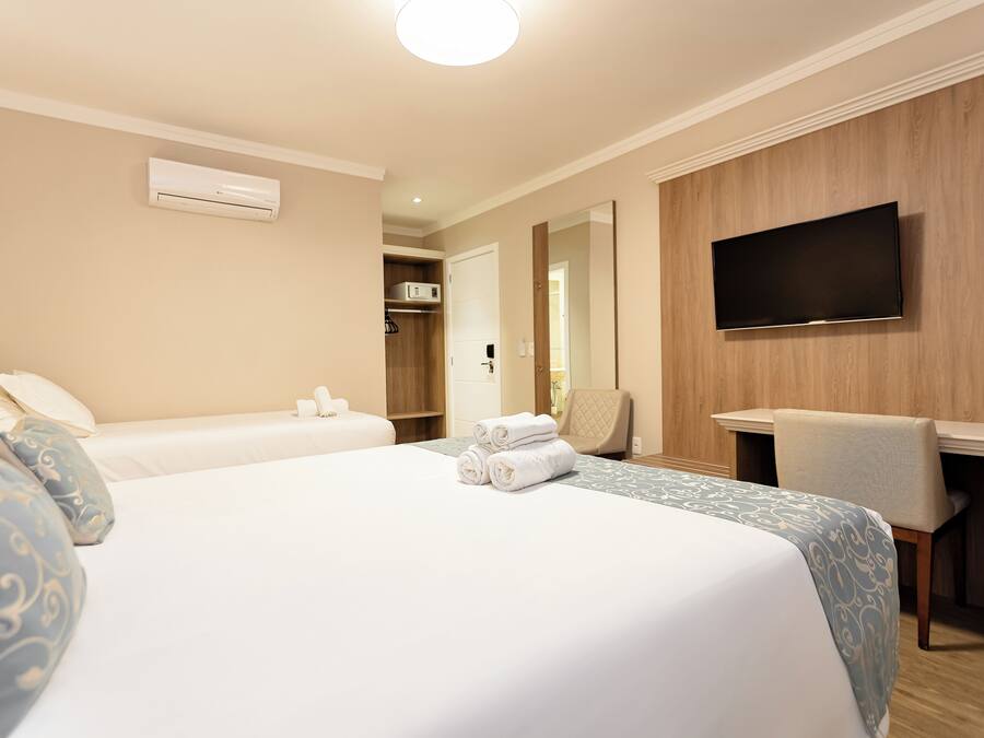 Quarto de hotel com uma cama grande, uma escrivaninha, uma cadeira, uma televisão e um ar condicionado.