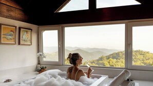 Uma mulher relaxa em uma banheira com vista para montanhas através de grandes janelas.