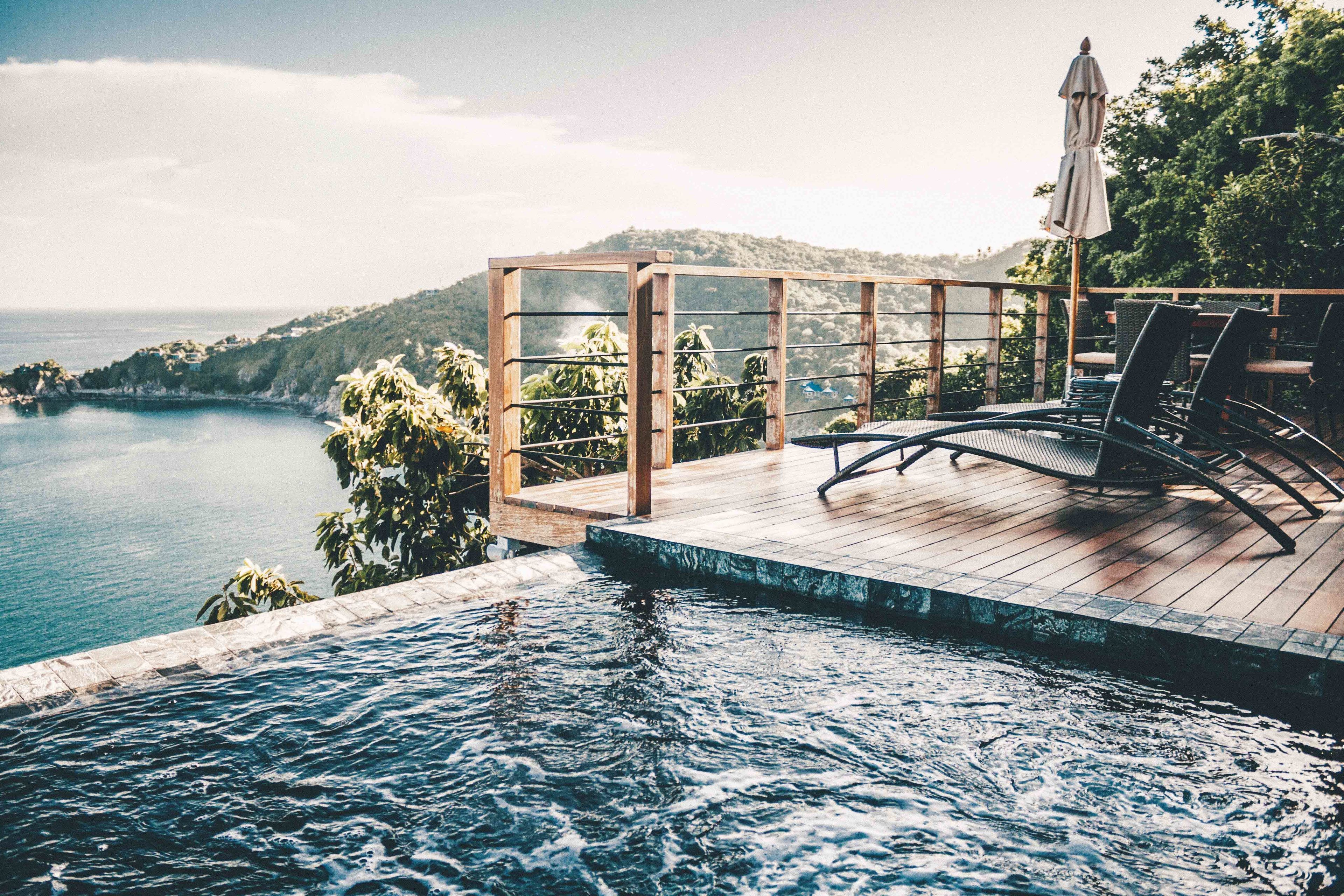 Uma piscina infinita com um deck de madeira, espreguiçadeiras e um guarda-sol.