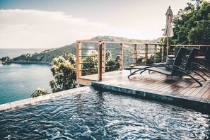 Uma piscina infinita com um deck de madeira, espreguiçadeiras e um guarda-sol.