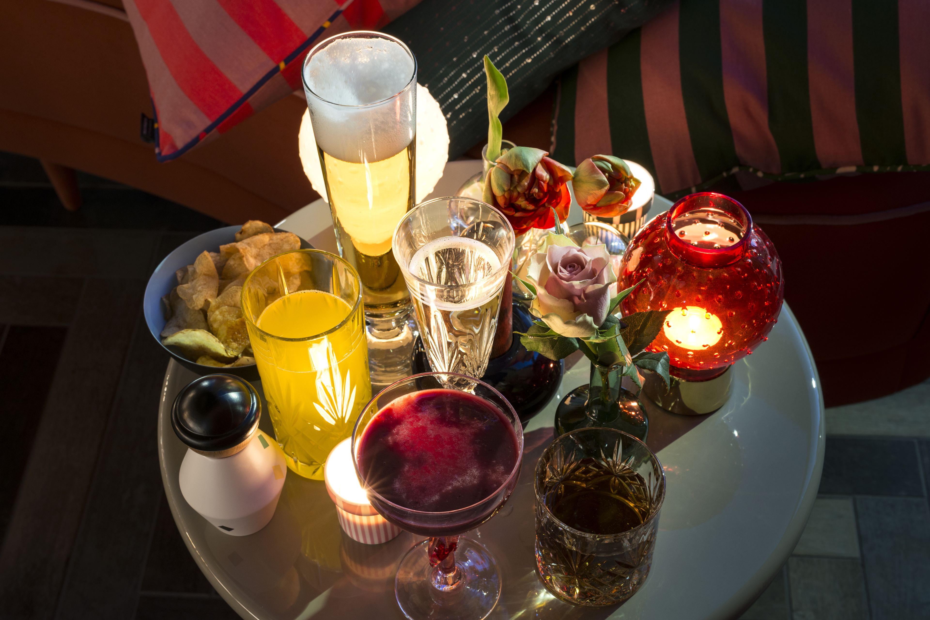 Uma bandeja com diversas bebidas, petiscos e objetos decorativos, incluindo uma vela e um copo com bebida vermelha.