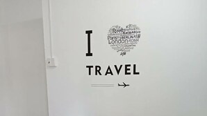 Quarto com uma cama, parede com uma nuvem de palavras sobre viagens e um pequeno baú de madeira.
