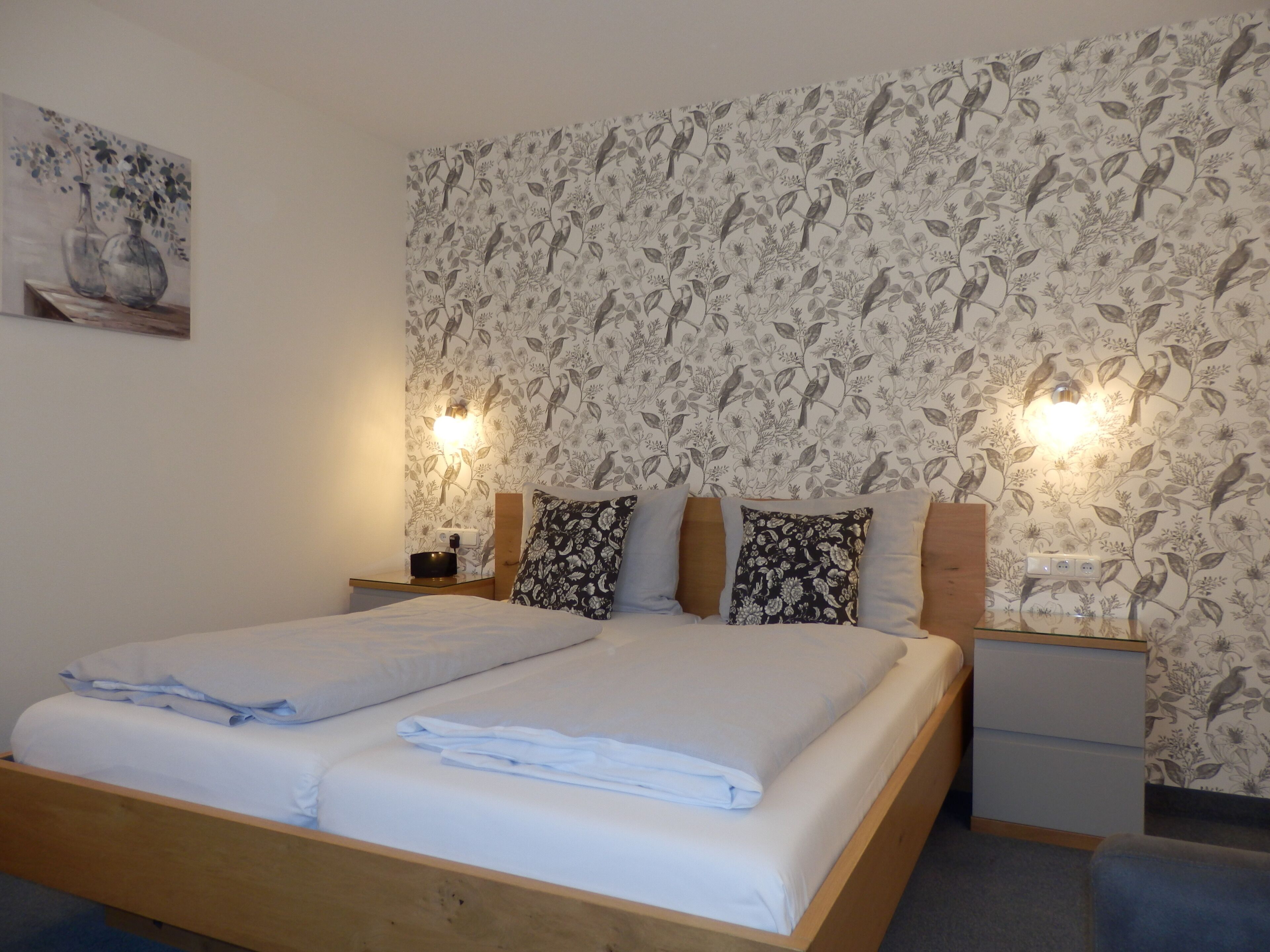 Quarto com cama, mesas de cabeceira e parede decorada com papel de parede floral.