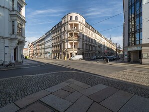 Um edifício histórico com arquitetura clássica, uma rua de paralelepípedos e uma linha de elétrico.