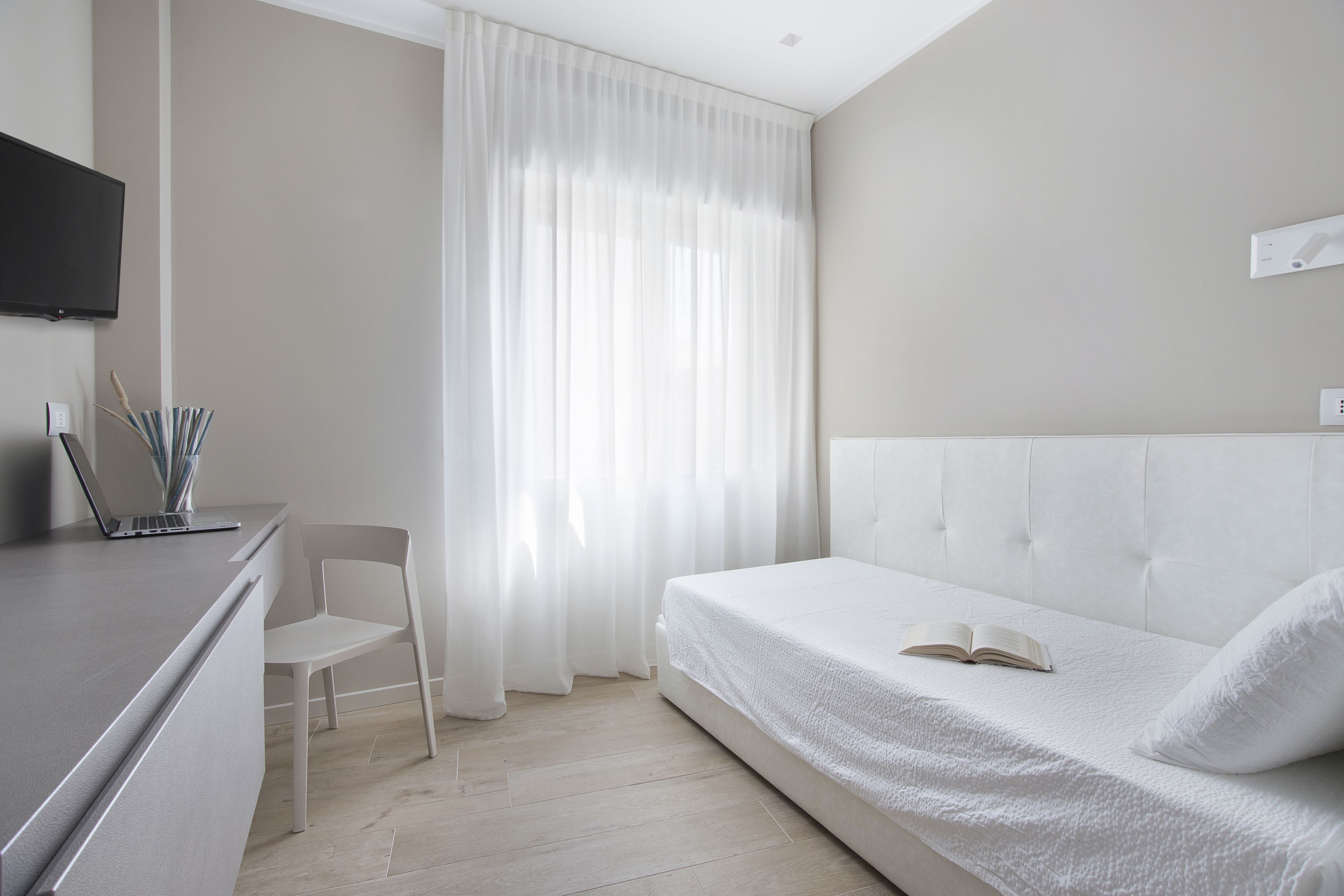 Quarto moderno com uma cama, uma escrivaninha com um laptop e uma cadeira.