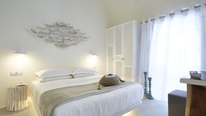 Um quarto com cama, luminárias de cabeceira, uma obra de arte na parede, mesa de cabeceira e uma janela com cortinas.