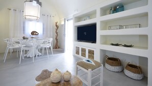Uma sala de estar moderna com um conjunto de jantar branco, uma televisão sobre uma estante branca e cestos decorativos.