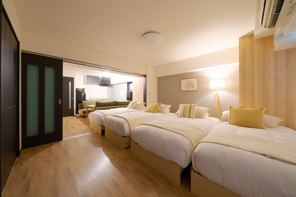Quarto de hotel com duas camas, um sofá, um espaço de refeições e uma cozinha ao fundo.