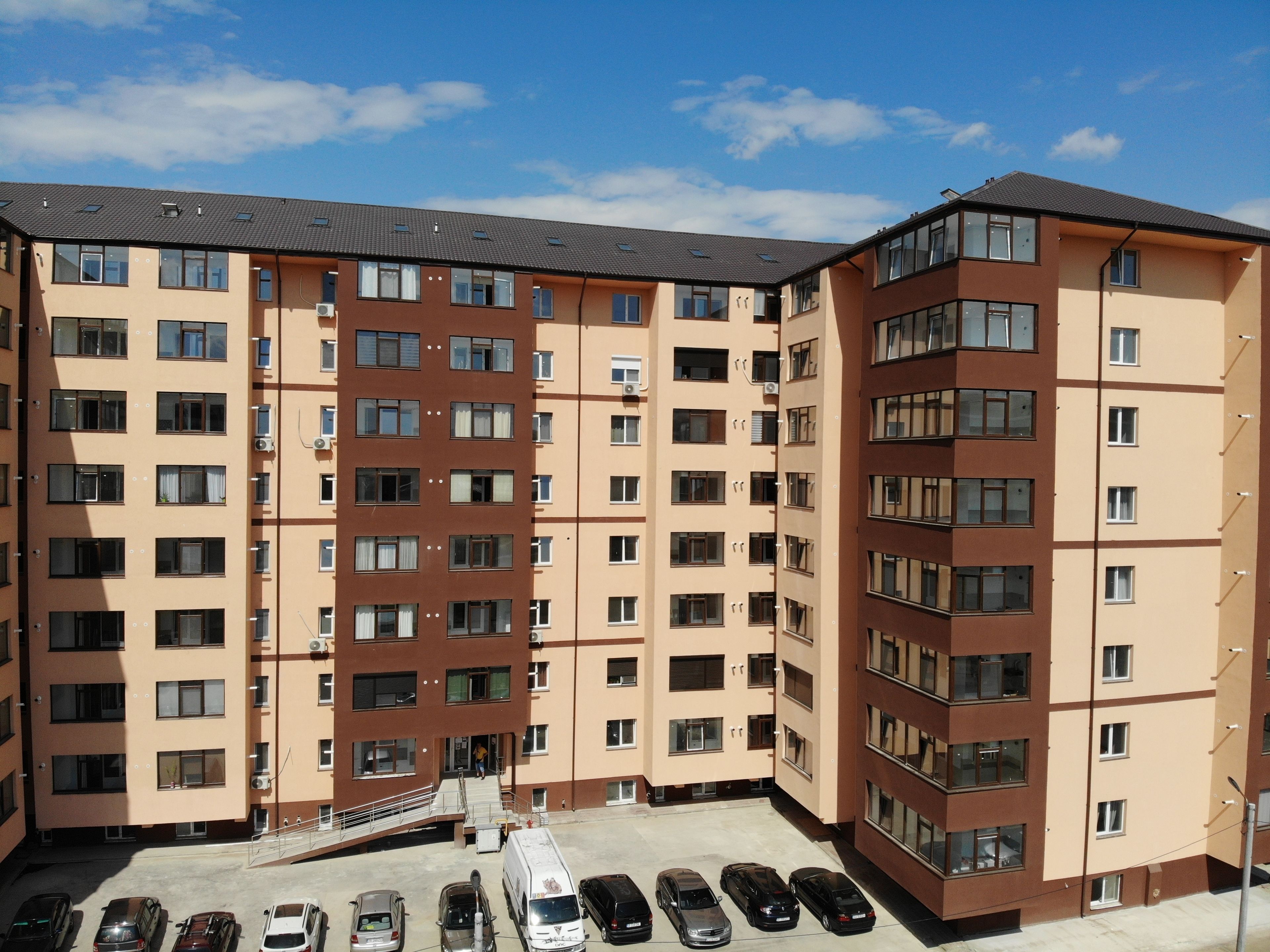 Um edifício residencial com vários andares e uma área de estacionamento em frente.