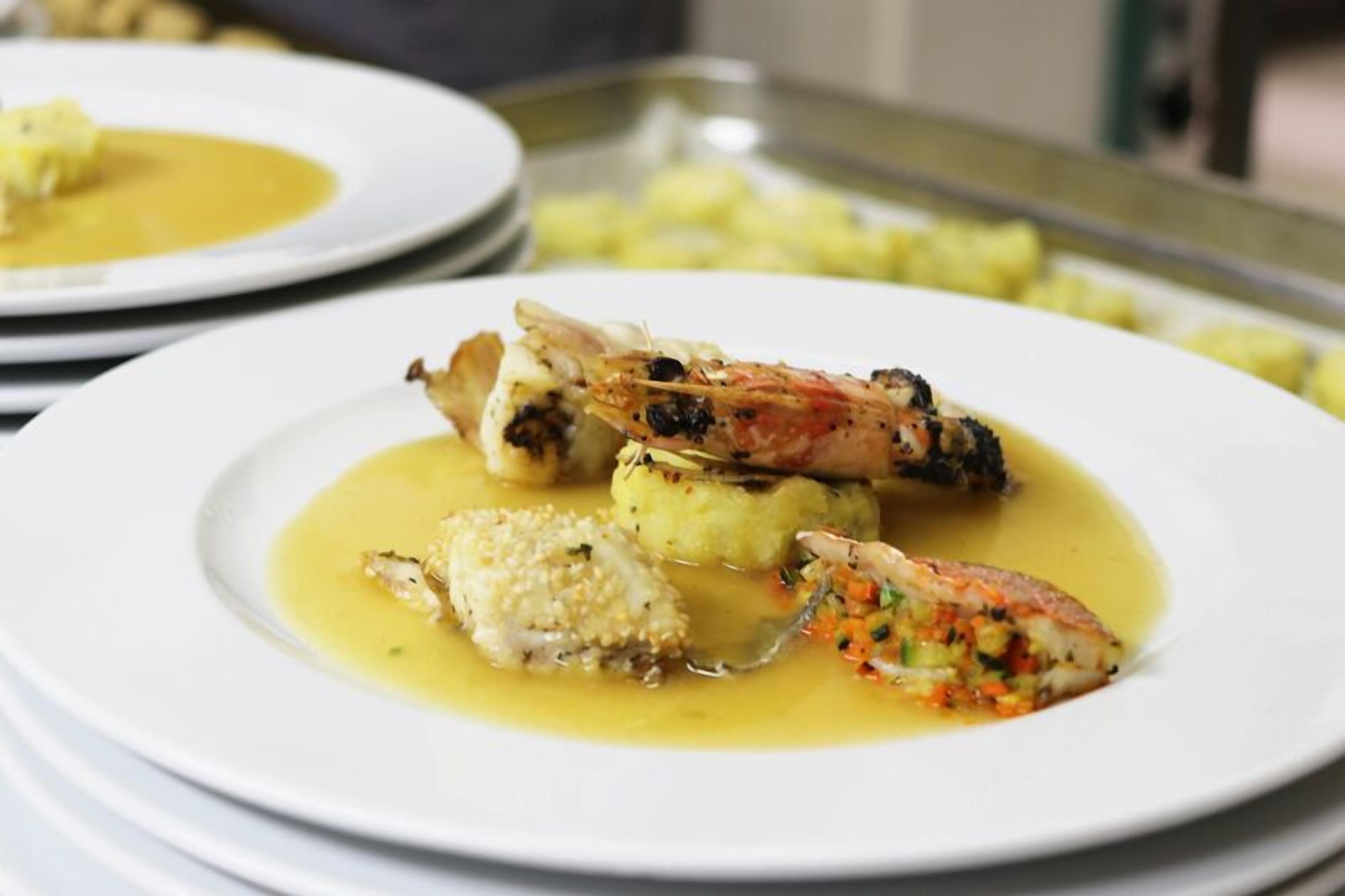 Prato com frutos do mar, incluindo um rabo de lagosta e peixe, acompanhado de molho amarelo.