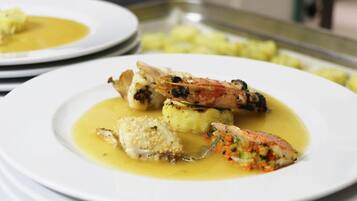 Prato com frutos do mar, incluindo um rabo de lagosta e peixe, acompanhado de molho amarelo.