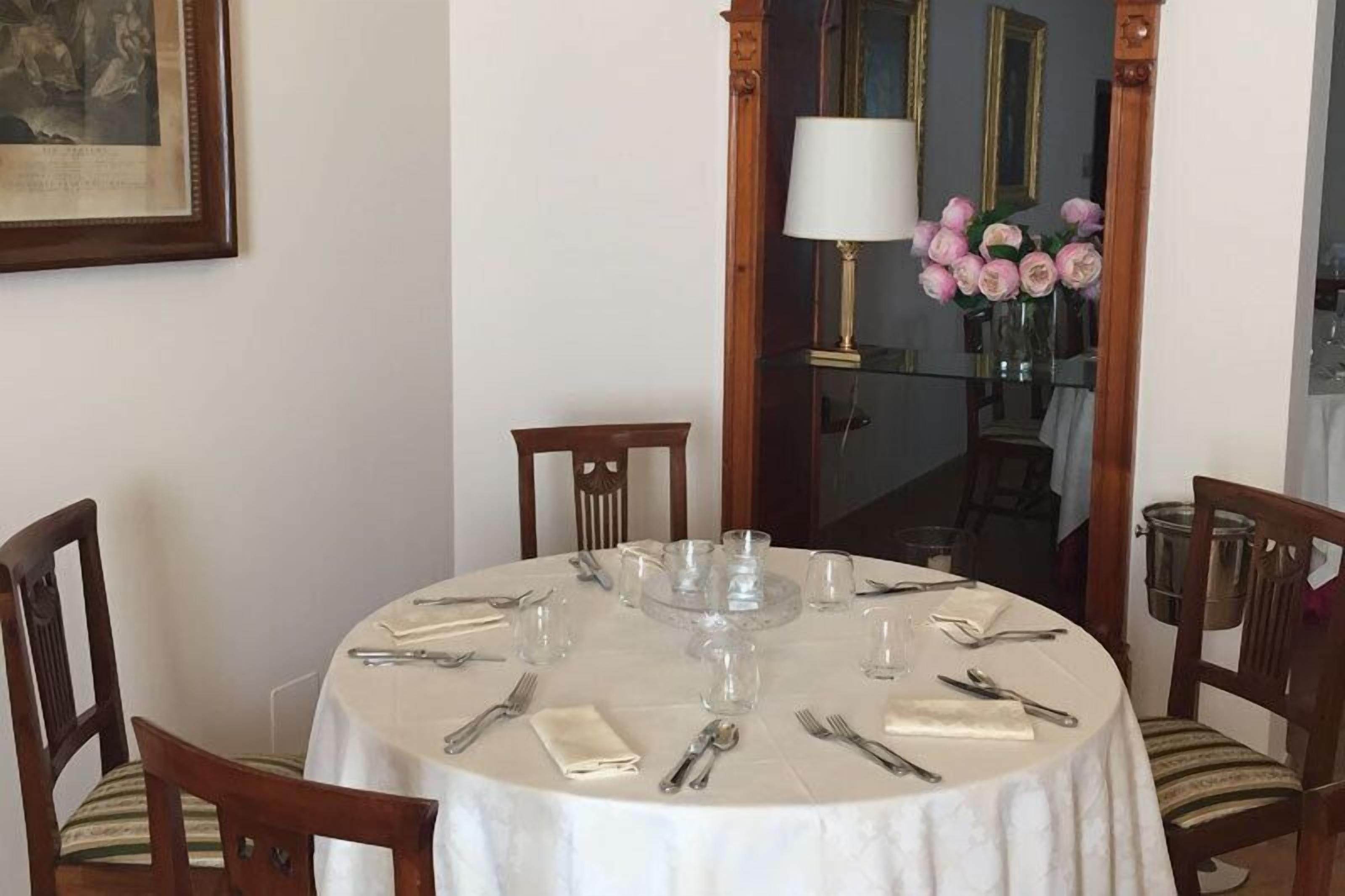 Mesa de jantar posta para quatro com cadeiras, um espelho, um vaso de flores e um abajur.