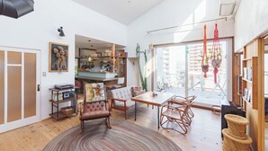 Uma sala de estar ampla com uma janela grande, uma área de jantar e uma cozinha visível por uma porta aberta.