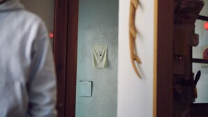 Um quarto com porta de madeira, interruptor de luz e luminária fixada na parede.
