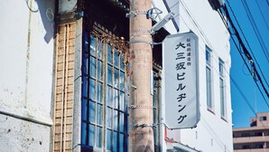 Um edifício com uma placa em japonês, uma janela de madeira com persianas e um poste de eletricidade com fios.