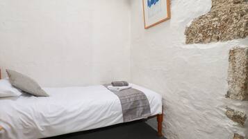 Uma cama de solteiro com colchão branco e cobertor cinza, travesseiro cinza e um quadro na parede.