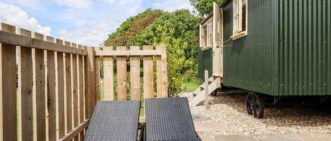 Um deck de madeira com uma rampa metálica que leva a um edifício verde com uma janela e uma porta.