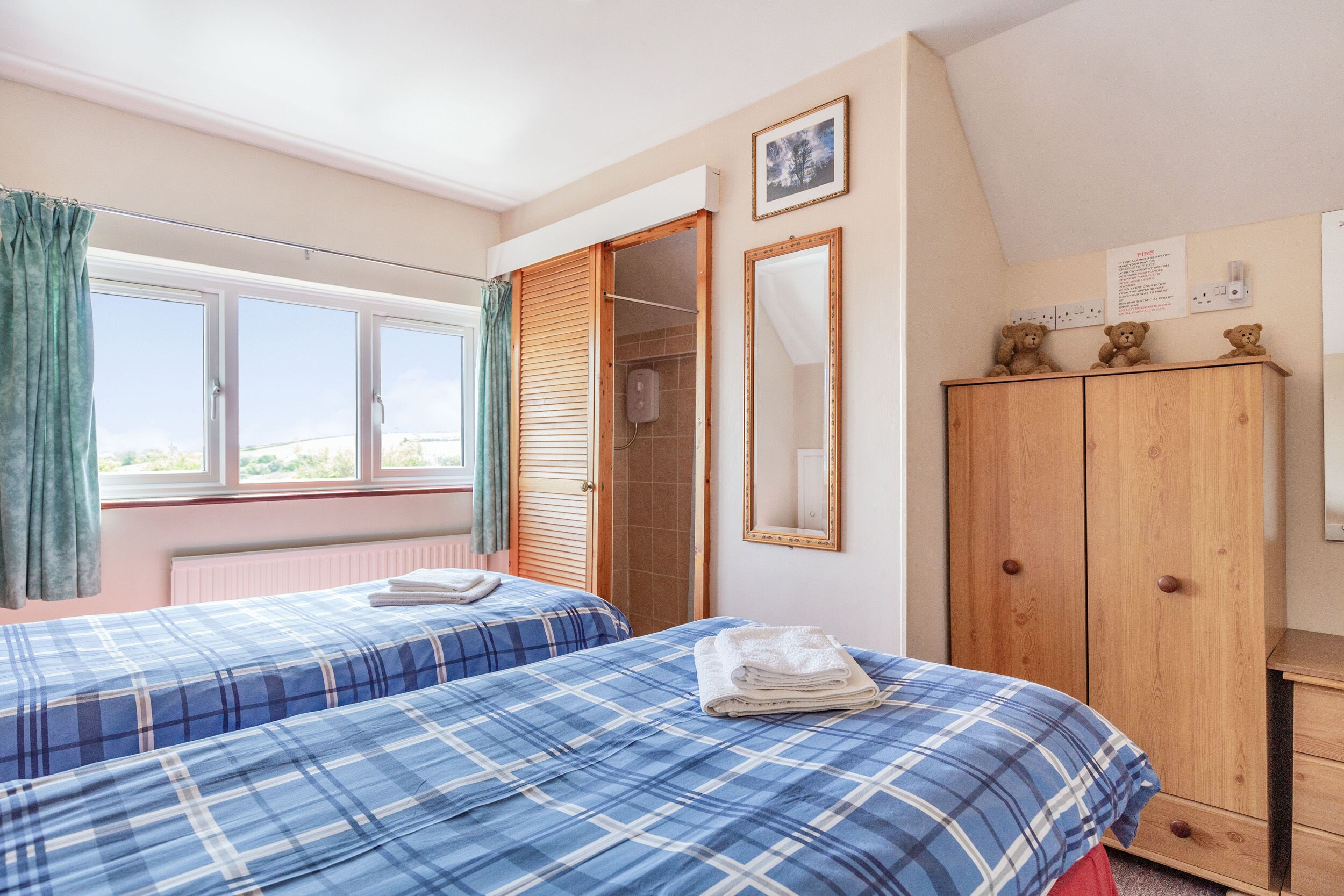 Quarto com duas camas, guarda-roupa de madeira, espelho e janela com cortinas.