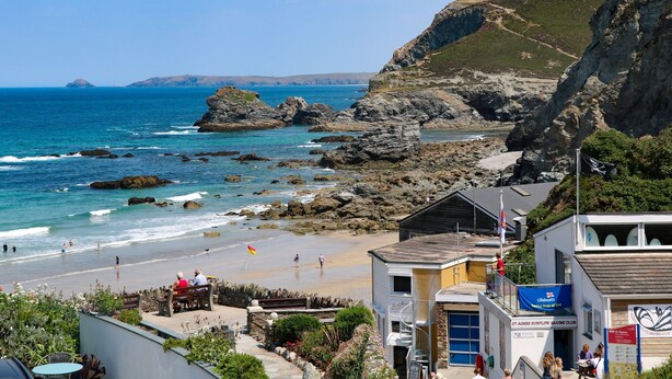 Vista costeira com falésias rochosas, uma praia e um edifício com a placa 'St. Agnes Surplus Saving Club'.