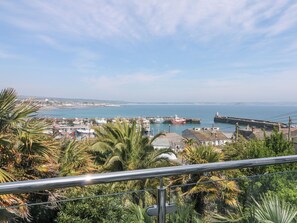 Uma vila costeira com um porto, barcos e um farol ao longe.