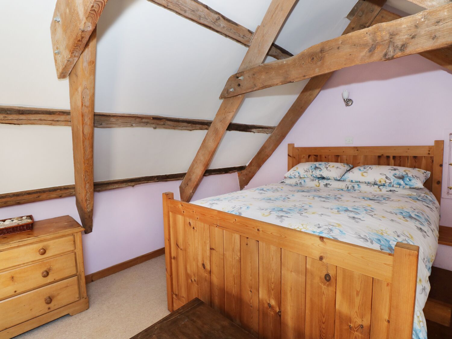 Quarto com cama de madeira, mesa de cabeceira e cómoda. O quarto apresenta vigas de madeira aparente no teto.