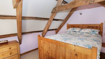Quarto com cama de madeira, mesa de cabeceira e cómoda. O quarto apresenta vigas de madeira aparente no teto.