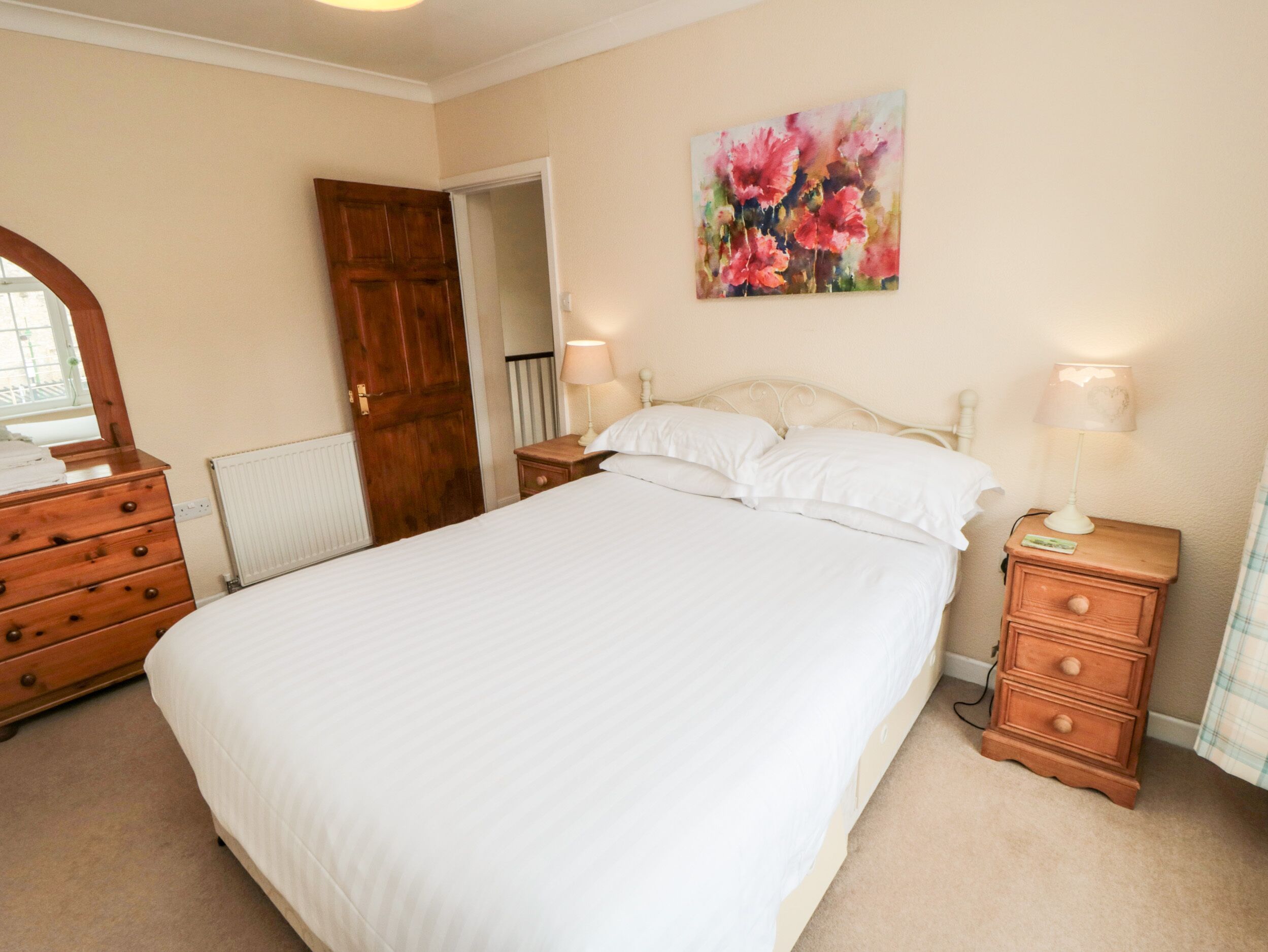 Quarto com uma cama grande, cómoda de madeira e uma pintura na parede.