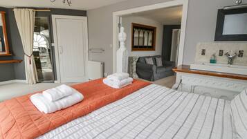 Quarto de hotel com uma cama grande, penteadeira, espelho, janela com cortinas e porta que dá para outro cômodo.