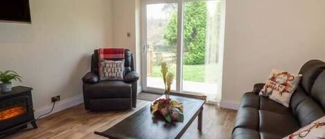 Uma sala de estar com lareira, sofá, mesa de centro e porta de vidro deslizante para um jardim.