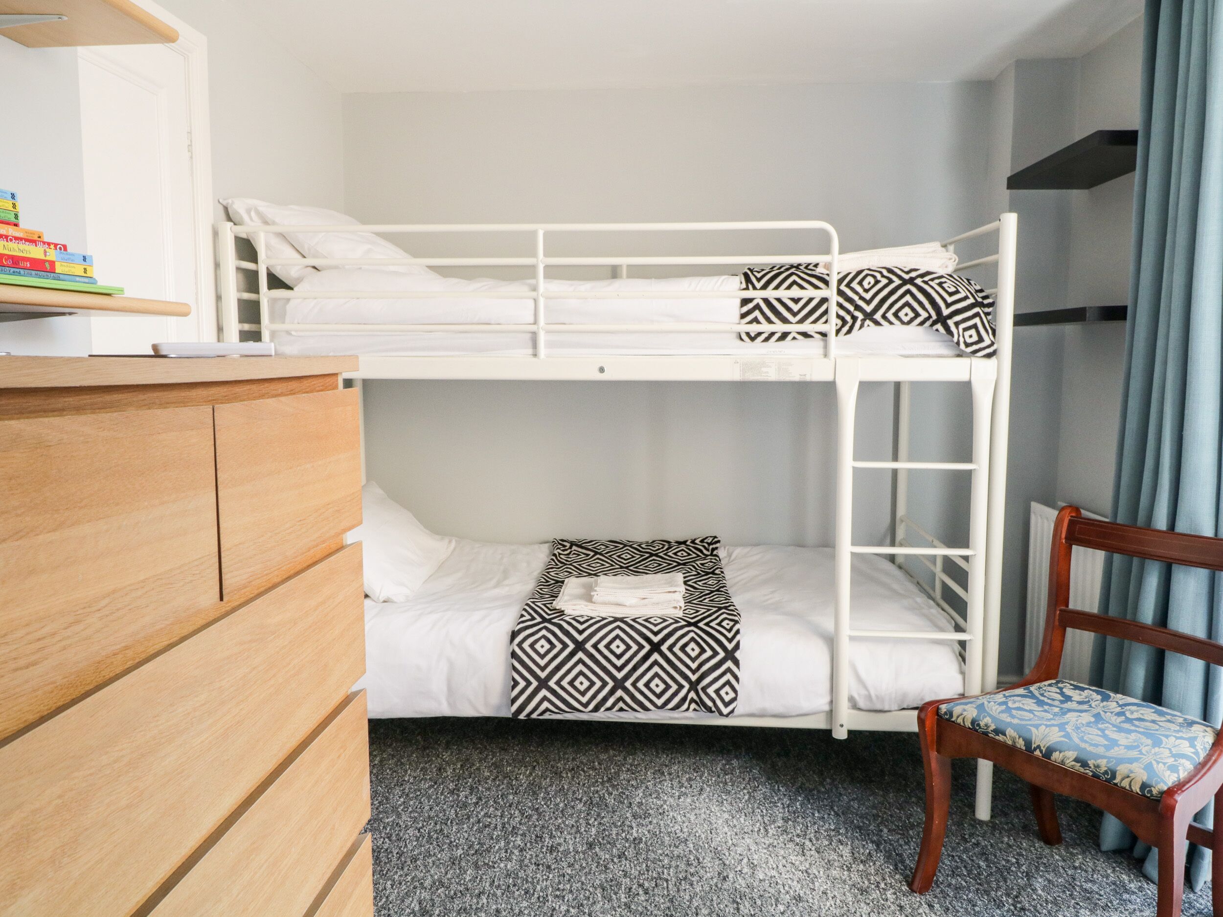 Quarto com beliche, cômoda de madeira, uma cadeira e uma estante de livros.