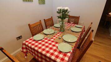 Mesa de jantar posta com pratos, copos e talheres, rodeada por cadeiras de madeira.