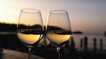 Duas taças de vinho sobre uma mesa de madeira, com vista para o pôr do sol ao fundo.