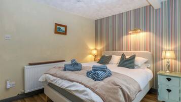 Quarto com cama, luminárias de cabeceira, radiador, parede listrada e pequena mesa de cabeceira.