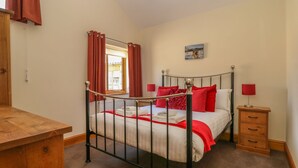 Quarto com estrutura de cama em metal, cómoda de madeira, mesa de cabeceira com abajur e janela com cortinas.