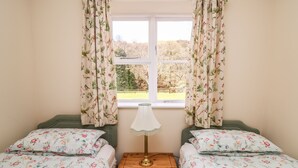 Quarto com duas camas de solteiro, uma mesa de cabeceira de madeira, um abajur e uma janela com cortinas florais.