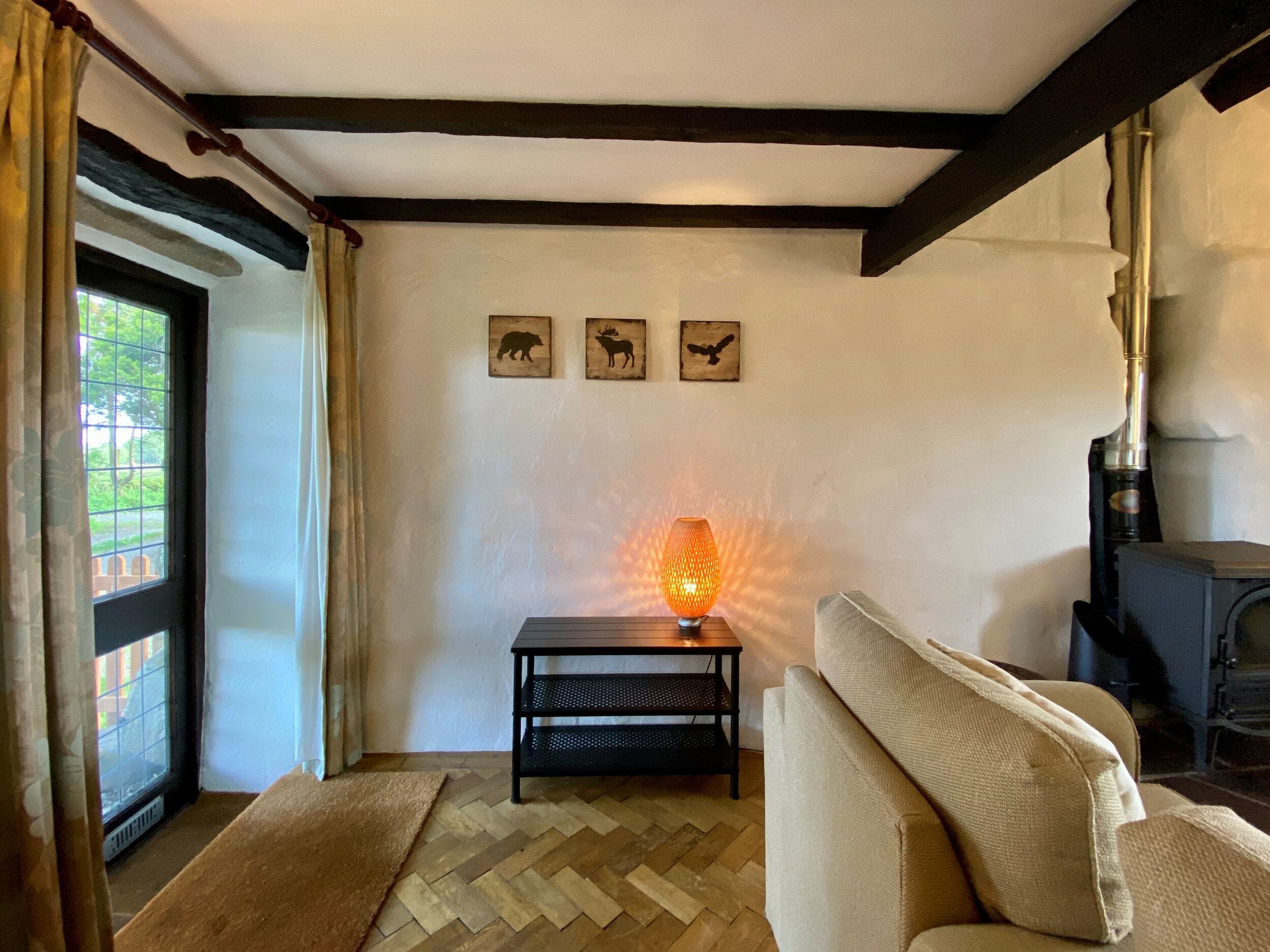 Um quarto aconchegante com piso em padrão herringbone, um sofá, uma mesa com abajur e três quadros de animais na parede.